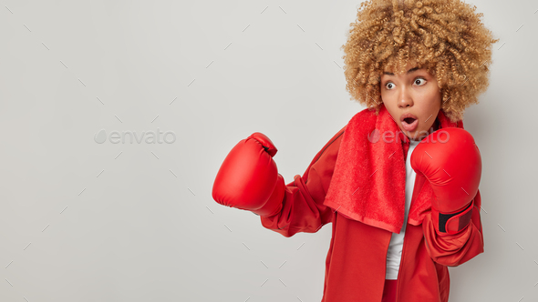 Shocked woman with curly hair ready for fight clenches fists wears red ...