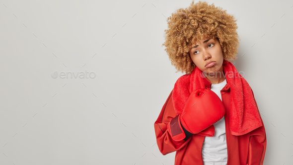 Sad tired sportswoman rests after boxing practive looks unhappily aside ...