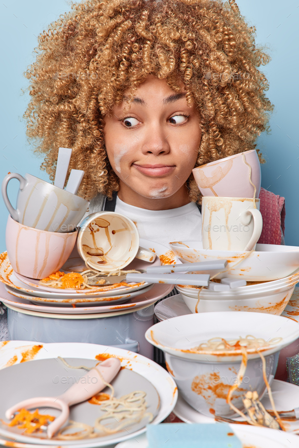 Headshot of surprised curly haired woman looks with wonder at pile of ...