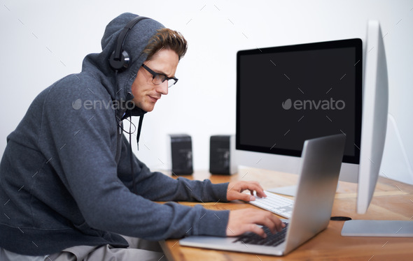 Engrossed in his work. A young hacker working on dual screens and a ...