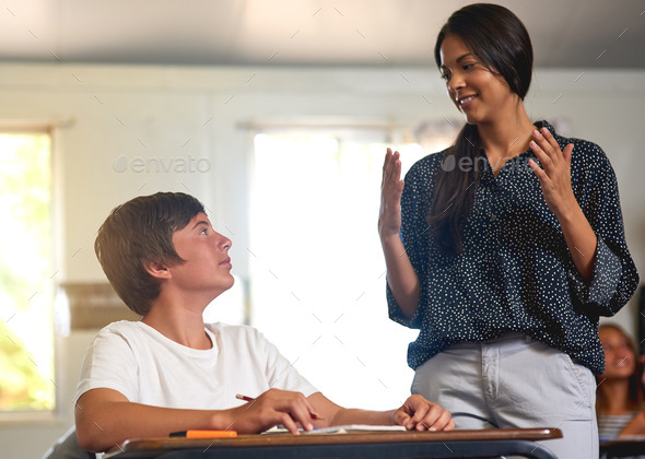 Shot of a young teacher explaining something to a student in her class ...