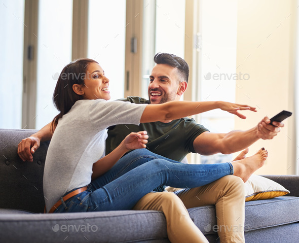 Shot of a young couple fighting over the remote control while watching ...