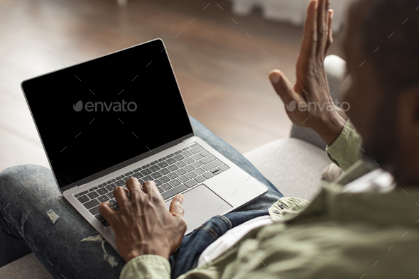 Happy adult black man using computer with blank screen, waving hand at ...