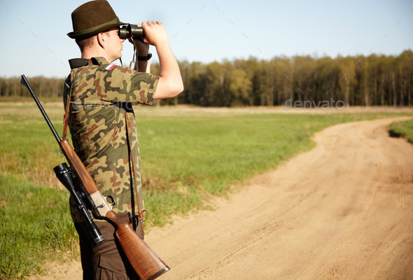 A game ranger with his rifle looking through his binoculars in the ...