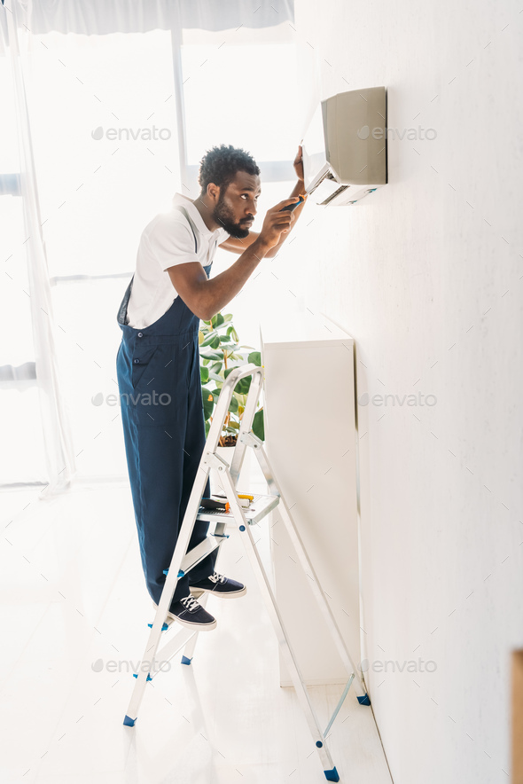 back view of african american repairman standing on ladder and fixing ...