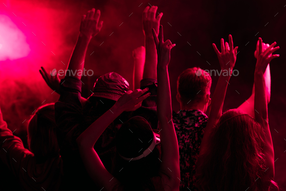 back view of people with raised hands during rave party in nightclub ...