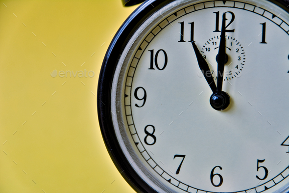 Shot of vintage retro analog clock on yellow background showing 11 o ...