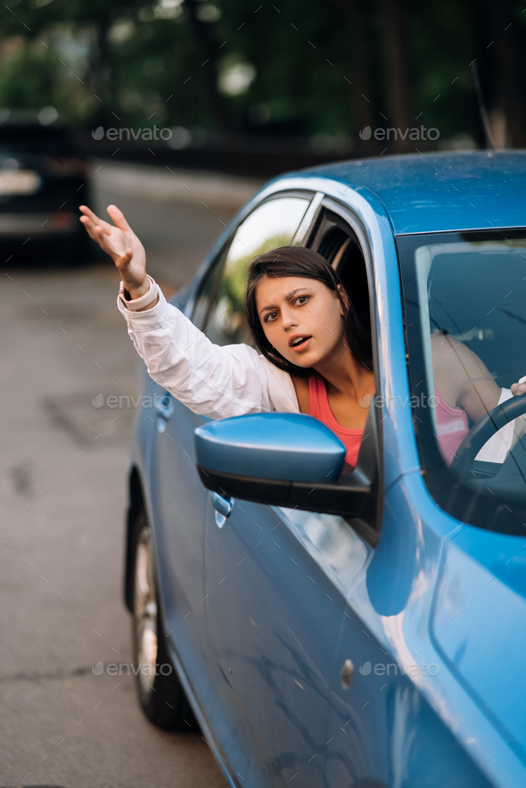 A young angry woman peeks out of the car window Stock Photo by simbiothy