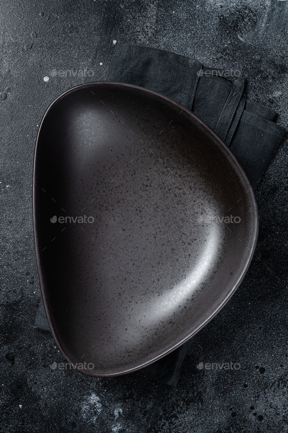 Empty black craft plate on table. Table setting. Black background. Top ...