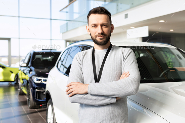 car dealership worker next to a new car looking at the camera with a ...