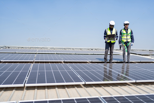 Engineer on rooftop stand next to solar panels discussion with team ...