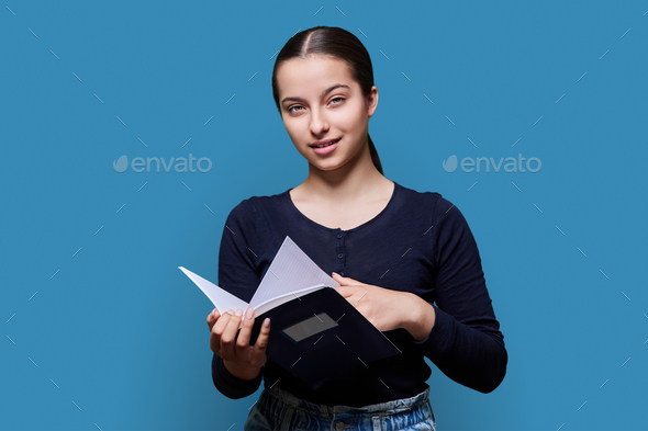 Teenager female student with notebook looking at camera on blue ...