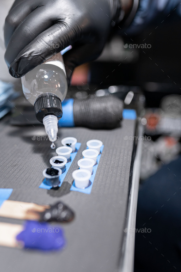 Close up of a tattoo artist is pouring ink into the plastic cups before ...