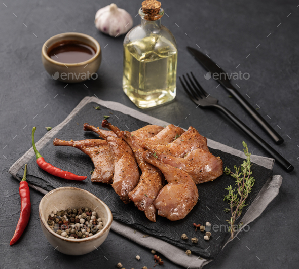 Grilled BBQ quail legs in marinade and spices on black slate with fresh ...