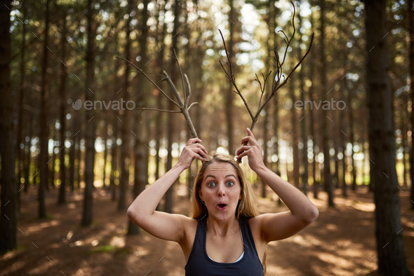 Portrait of a playful young woman holding tree branches up like antlers ...