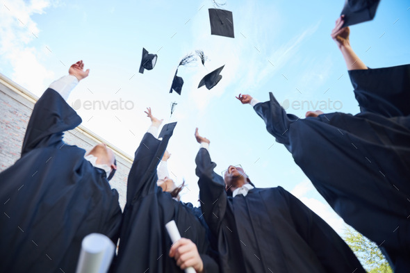 Low angle shot of a group of students throwing their caps into the air ...