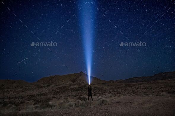 Man holding a flashlight to the sky on a starry night in deserted ...