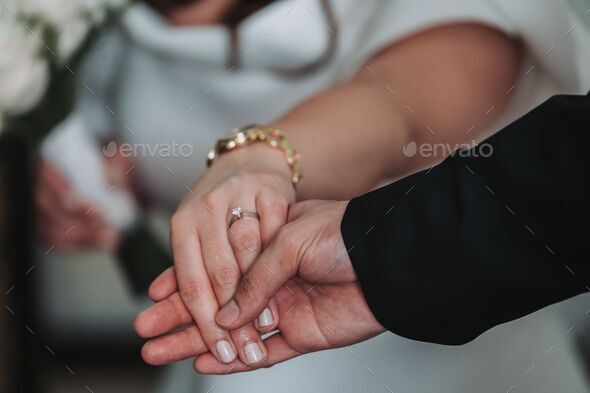 Closeup shot of the bride and the groom holding hands during the ...