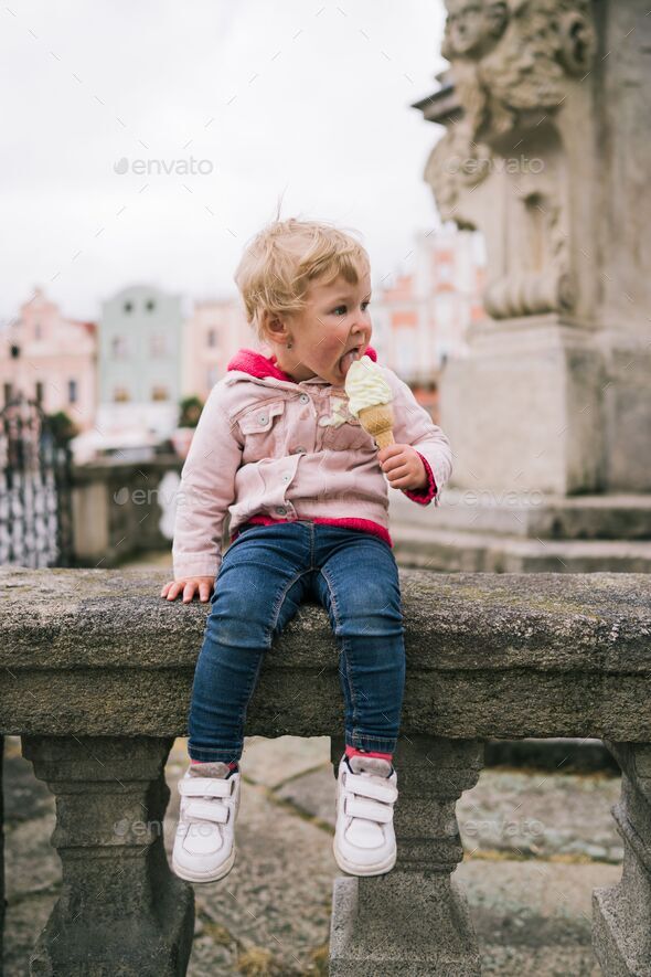 Vertical shot of a blonde caucasian little girl sitting on a stone ...