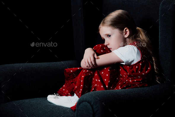 depressed, scared child sitting in armchair isolated on black Stock ...