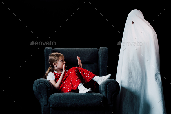direful ghost standing near scared girl sitting in armchair isolated on ...
