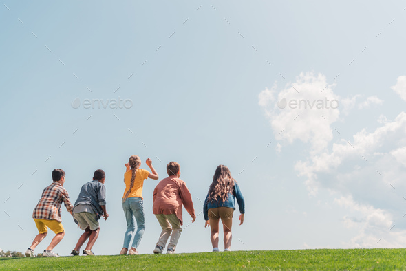 back view of multicultural kids jumping on green grass Stock Photo by ...