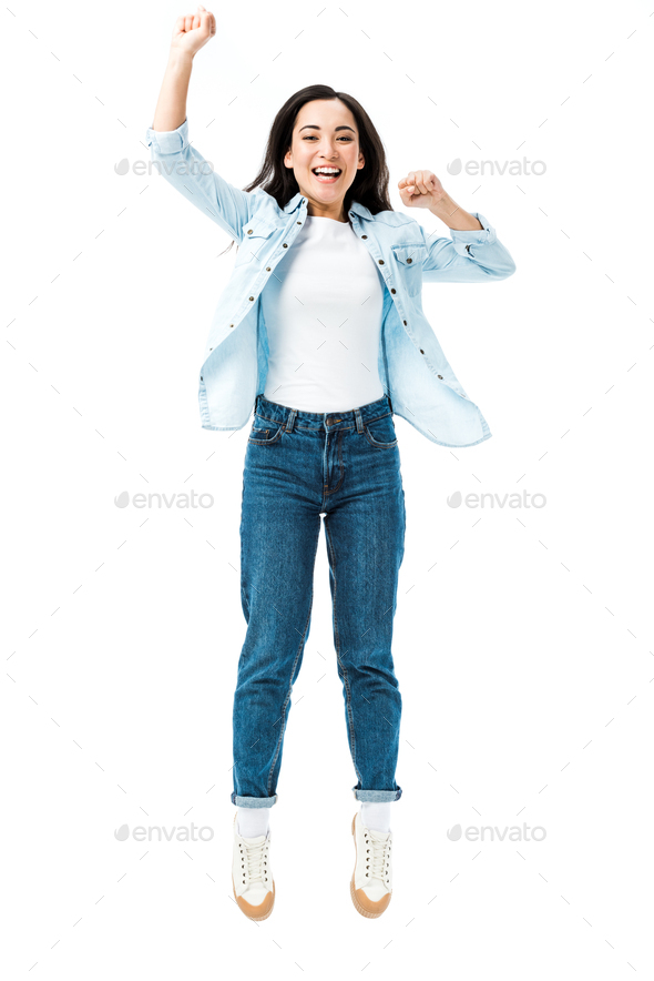 attractive and smiling asian woman in denim shirt jumping and showing ...