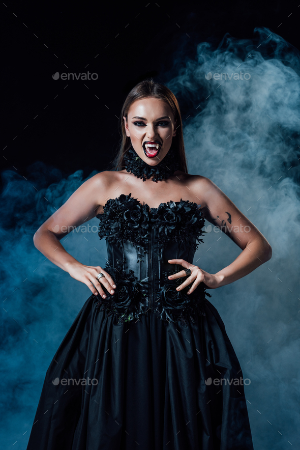 scary vampire girl with fangs in black gothic dress on black background ...