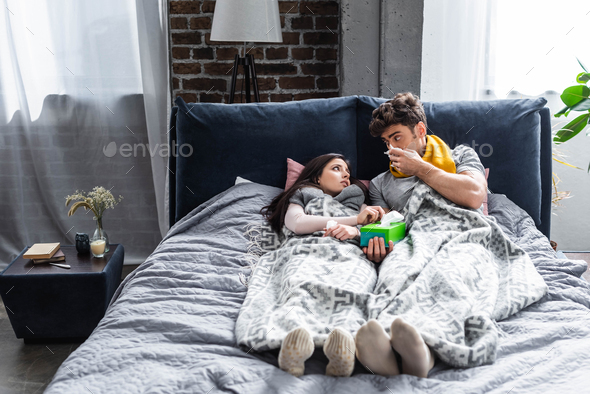 sick girlfriend and boyfriend sneezing and lying in bed Stock Photo by ...