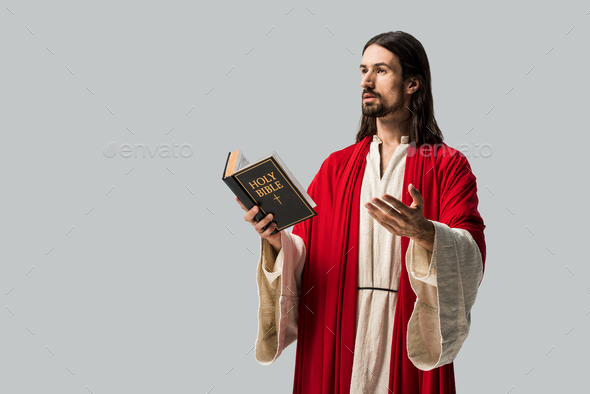 handsome man gesturing while holding holy bible isolated on grey Stock ...