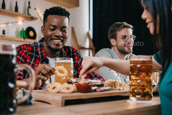 smiling multicultural friends eating fried onion rings with ketchup in ...