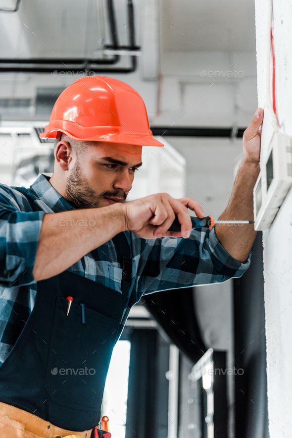 selective focus of handsome workman repairing control panel with ...