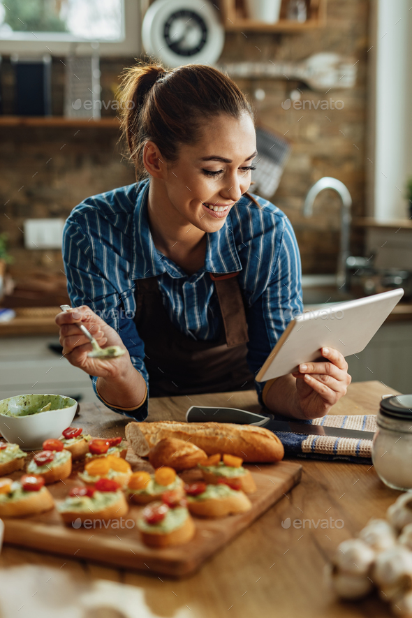 Happy woman following recipe on touchpad while making bruschetta in the ...