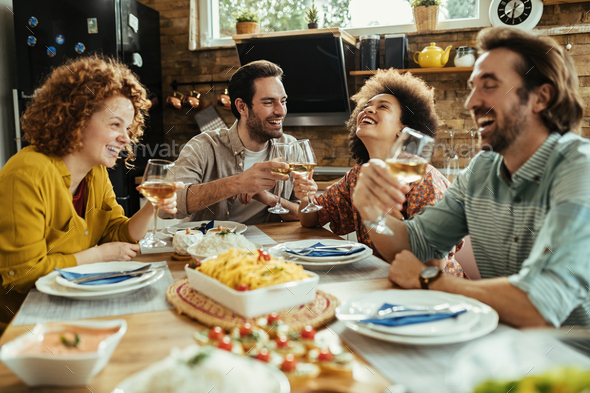 Happy young adults having fun while toasting with wine at dining table ...