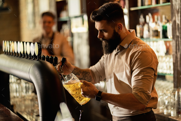 Young bartender pouring draft beer form beer tap in a pub. Stock Photo ...