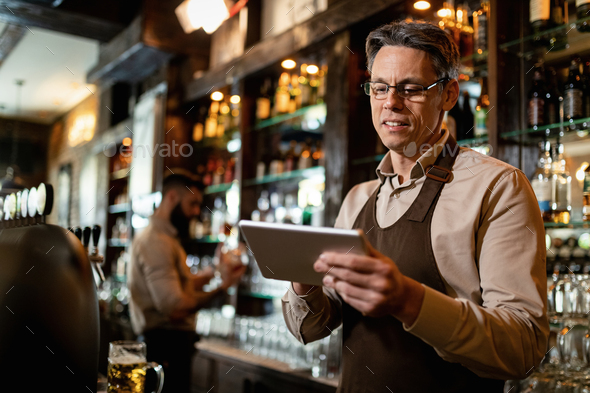 Smiling mid adult waiter using touchpad while working in a bar. Stock ...
