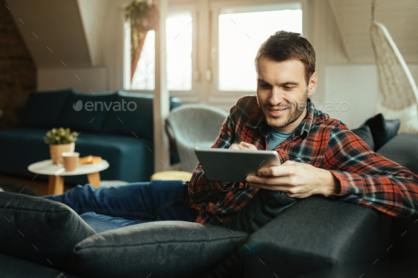 Happy man surfing the net on touchpad while relaxing in the living room ...