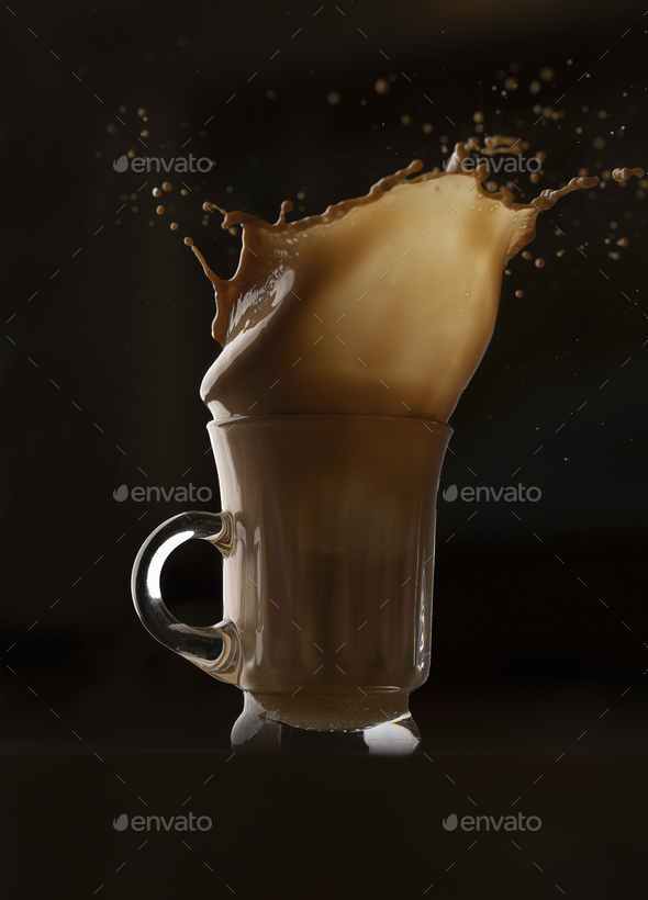 Vertical shot of a glass of karak tea splashed in the air on a black ...