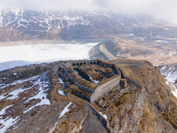 Ancient fort ruins in the mountains next to frozen lake and dam, aerial ...