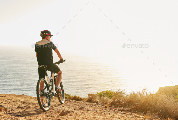 Shot of a man admiring the view from a hilltop while out on a bike ride ...