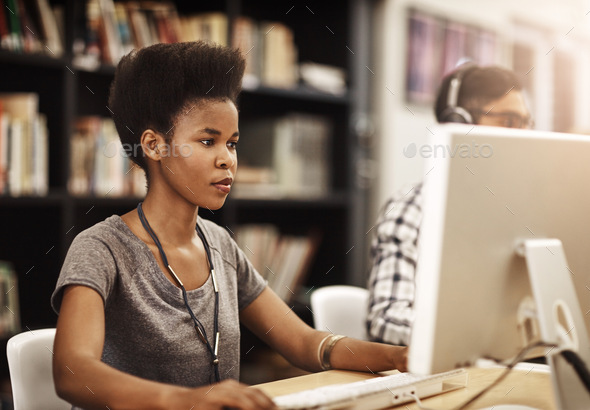 Shot of university students working on computers in the library on ...