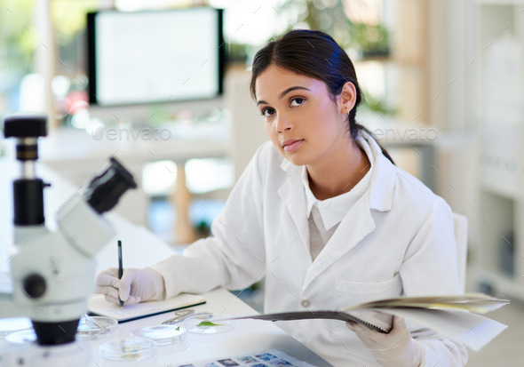 Portrait of a young scientist writing notes while working in a lab ...
