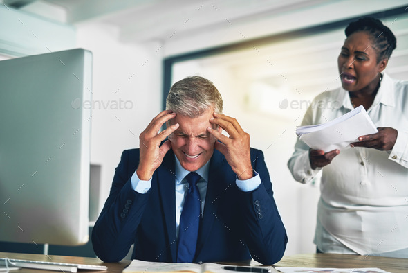 Shot of an angry businesswoman berating her colleague while he sits at ...