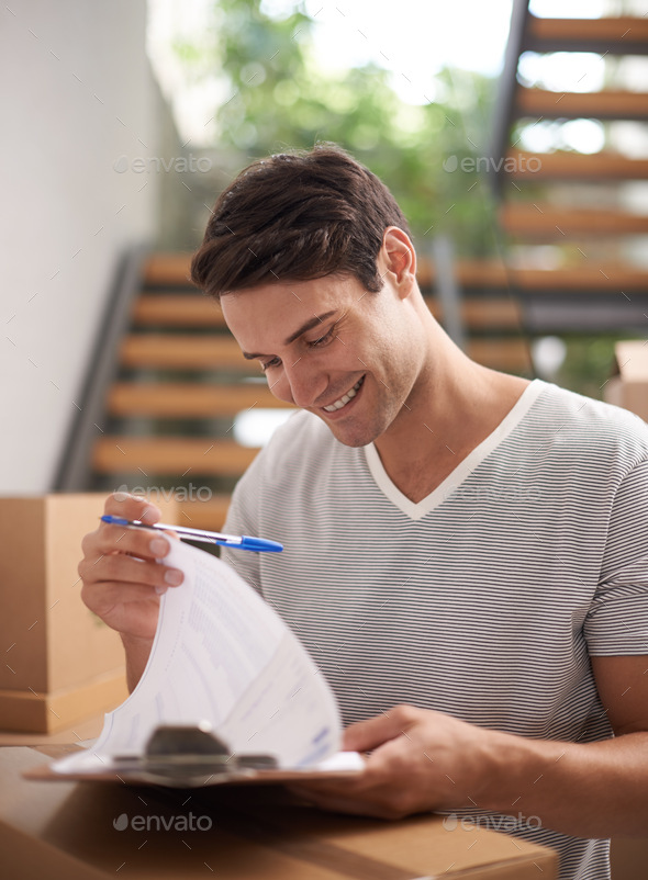 A happy young man signing for a delivery of packed cardboard boxes ...