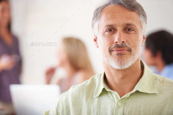 Handsome mature businessman looking composed with his coworkers blurred ...