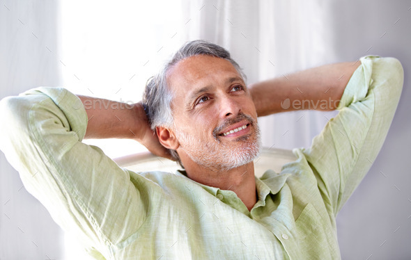 Laid-back. A mature man relaxing at home with his hands behind his head ...