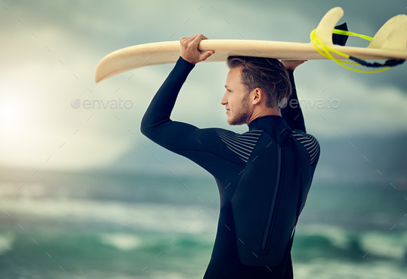 Shot of a laid-back young surfer watching the waves while holding his ...