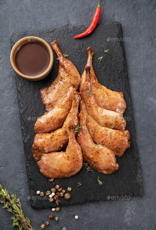 Delicacies. Grilled BBQ quail legs in marinade and spices on black ...