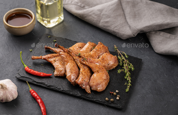 Grilled BBQ quail legs in marinade and spices on black slate with fresh ...