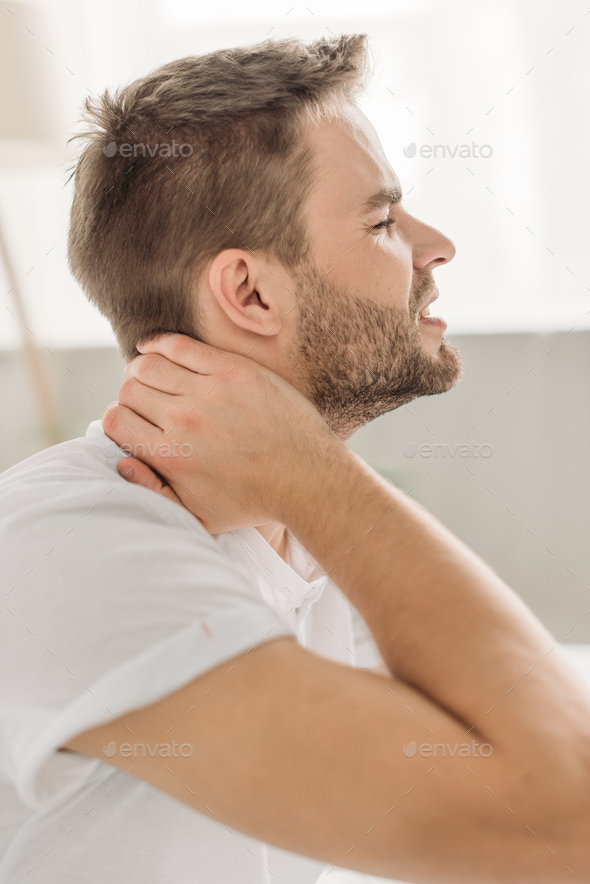 side view of young man touching neck while suffering from pain with ...